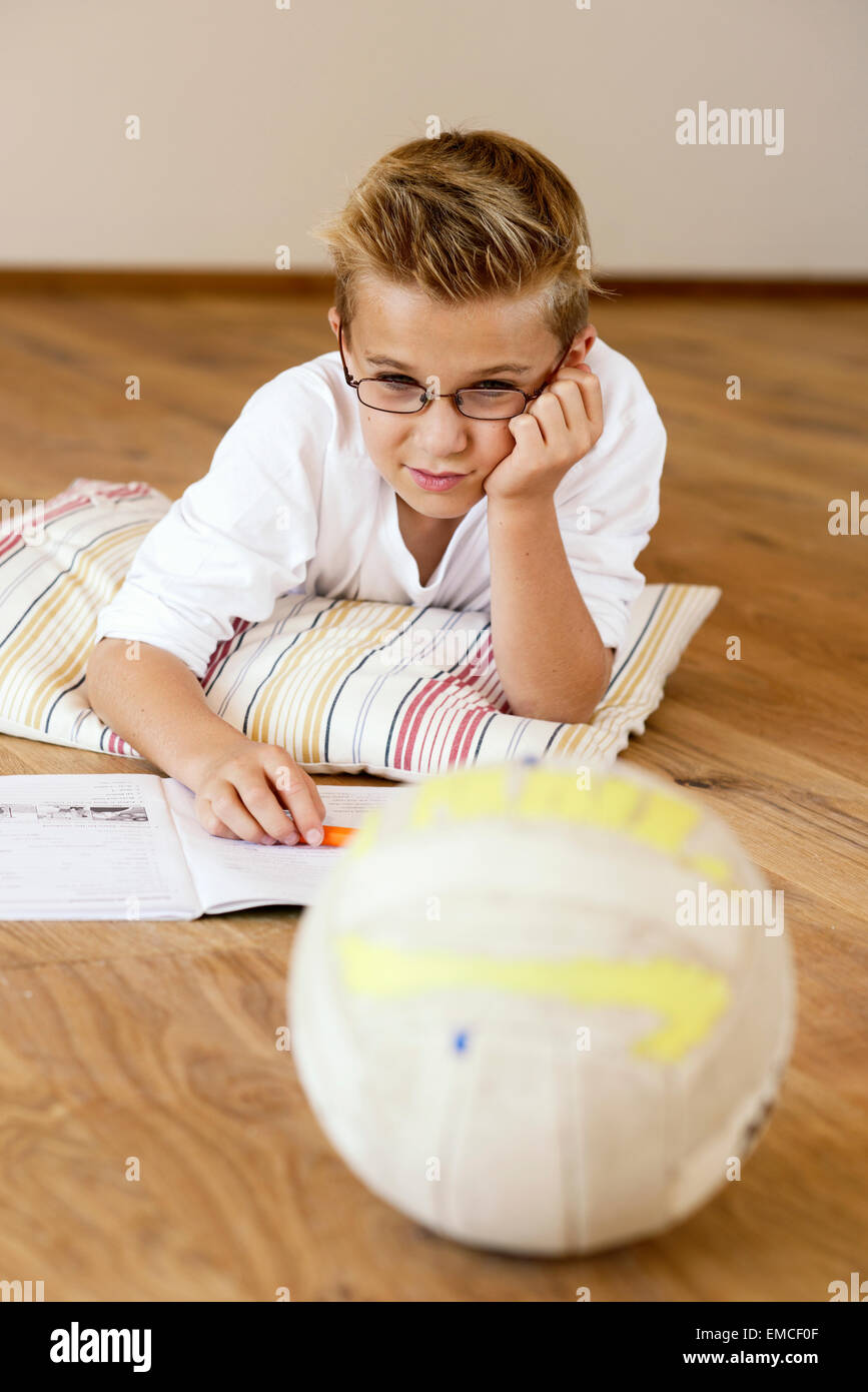 Boy doing homework on wooden floor looking at soccer ball Stock Photo ...