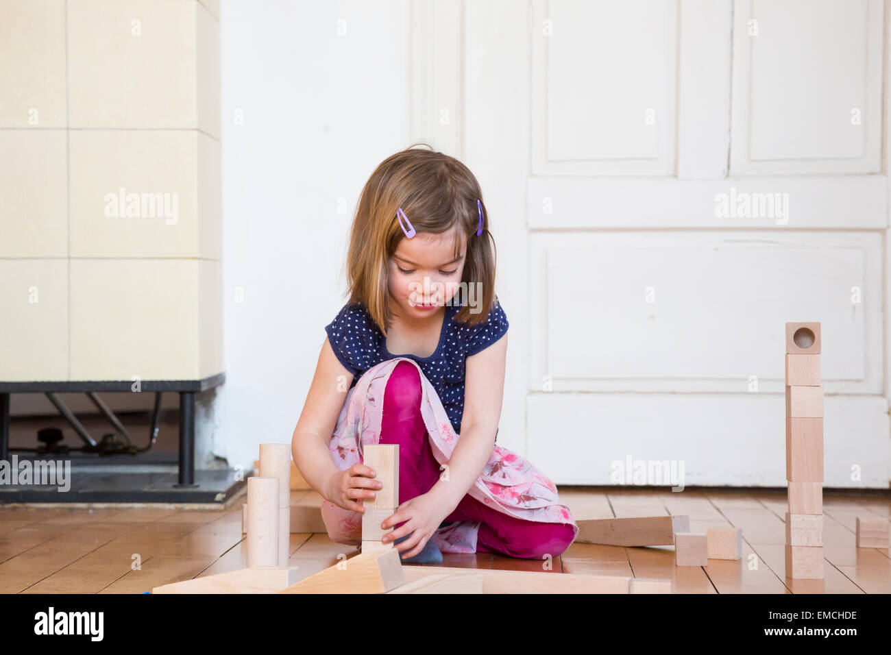 Little girl crouching on floor playing with wooden building bricks ...