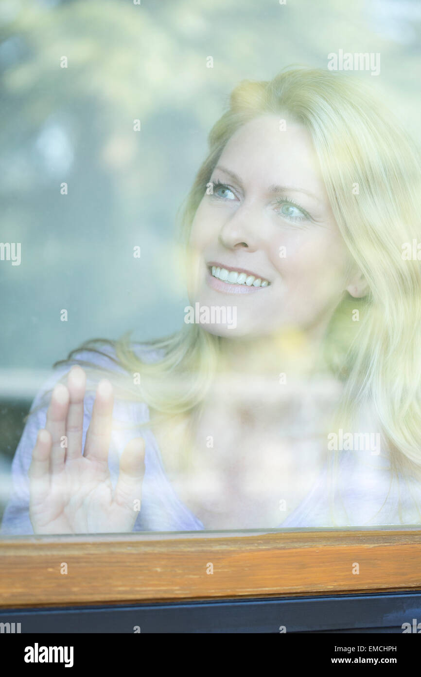 Blond woman looking through window Stock Photo - Alamy