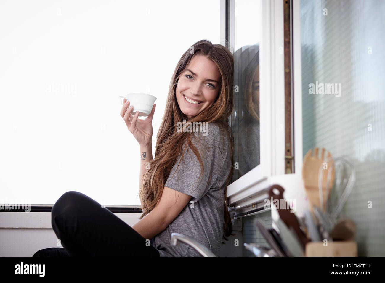 Young woman in kitchen sitting at window drinking coffee Stock Photo ...
