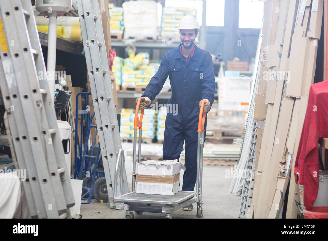 Warehouseman in storehouse pushing cart Stock Photo - Alamy