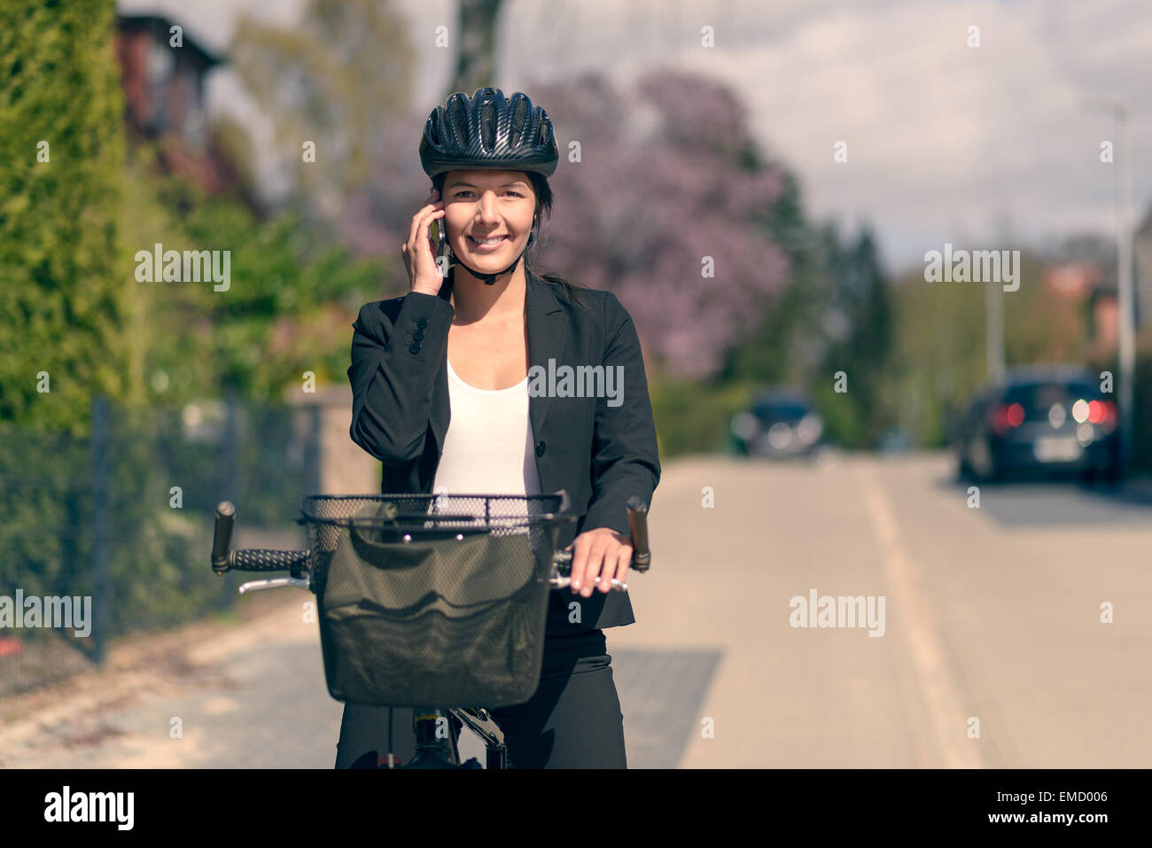 Stylish friendly young businesswoman riding to work pausing to answer a ...
