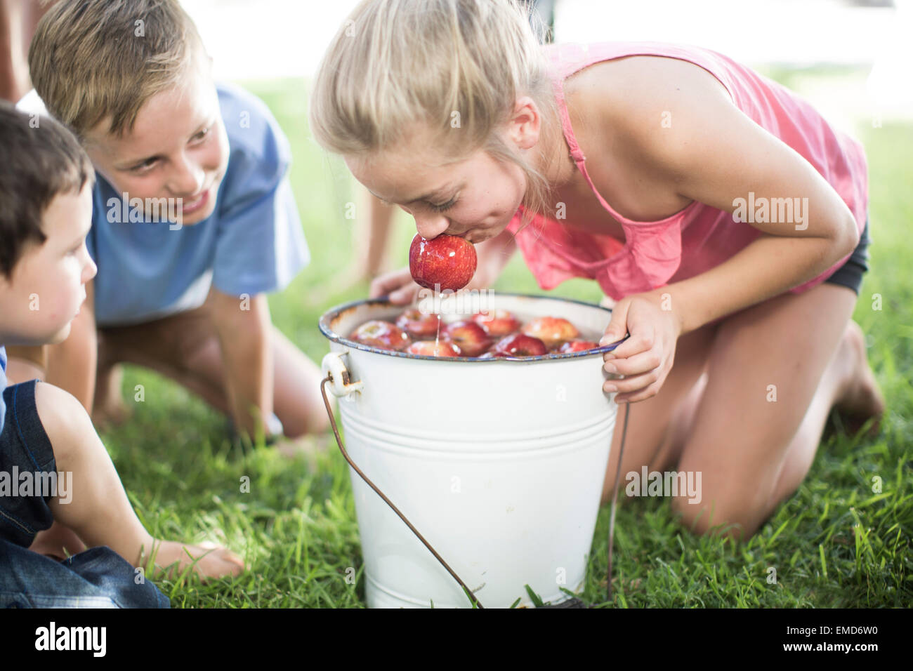 Girl trying to take apple out of bucket with water Stock Photo - Alamy