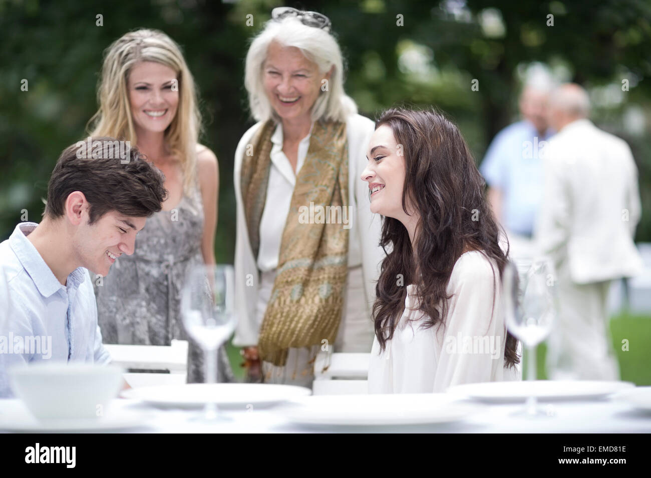 Happy family gathering around table in garden Stock Photo - Alamy