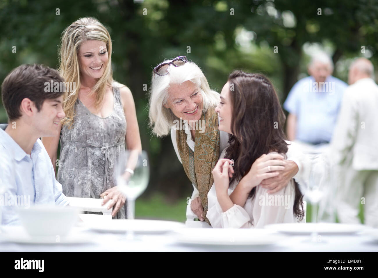 Happy family gathering around table in garden Stock Photo - Alamy