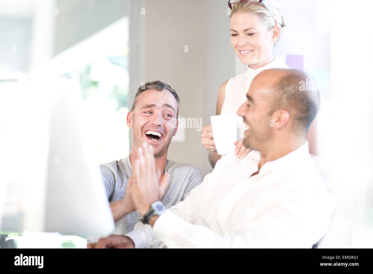 Co-workers gathering around computer screen in an office Stock Photo ...