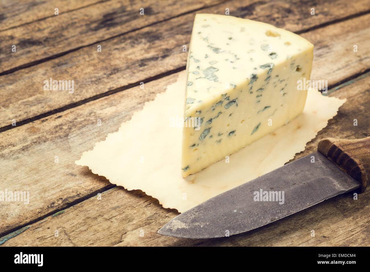 Blue cheese on old paper with rural knife on wooden table. Warm color ...