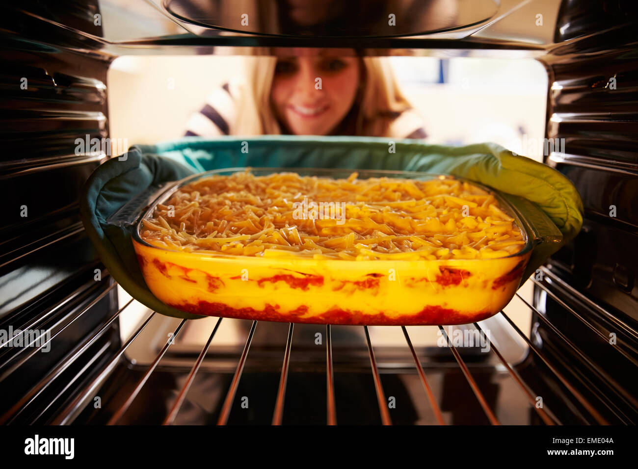 Woman Putting Dish Of Lasagne Into Oven To Cook Stock Photo - Alamy