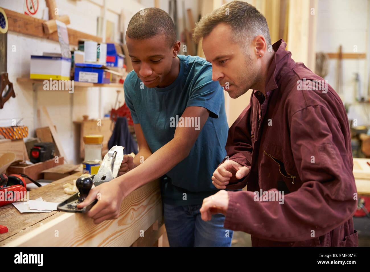 Carpenter With Apprentice Planing Wood In Workshop Stock Photo - Alamy