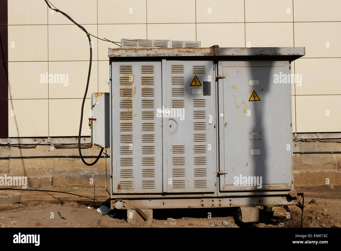 Electric high voltage transformer outdoors near wall of industrial ...