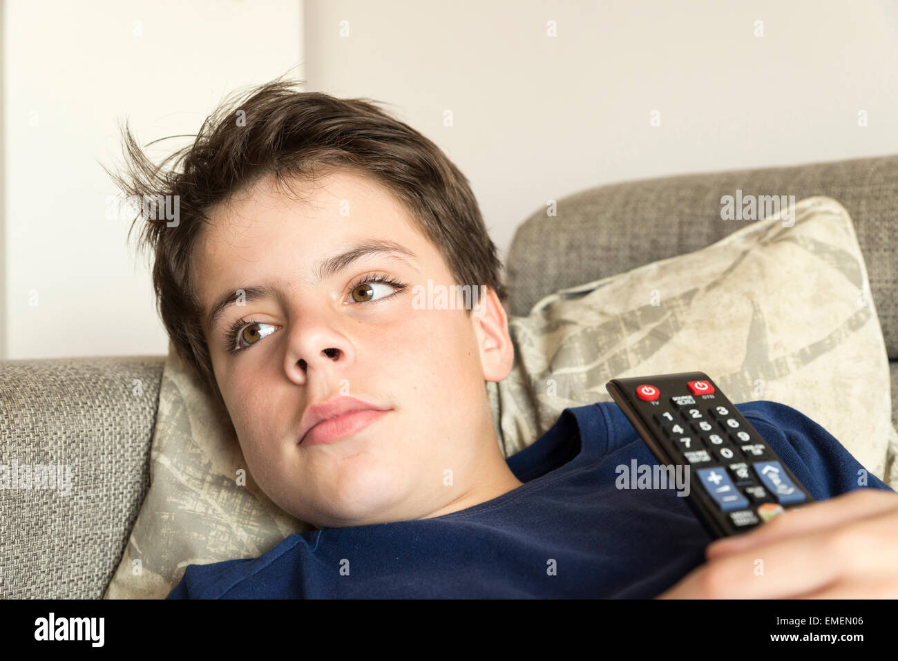Young boy with TV remote control watching TV on the couch stretched ...