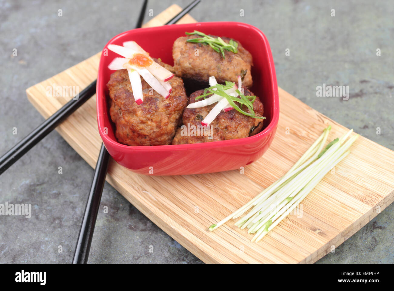Three meatballs with radish and parsley served in a red Asian bowl with ...