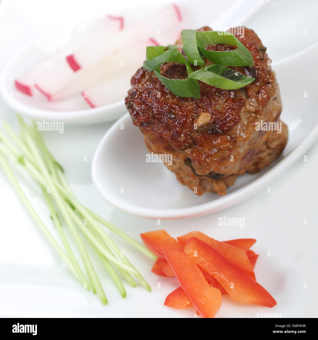 Single Asian style meatball served in a spoon, with sliced radish ...