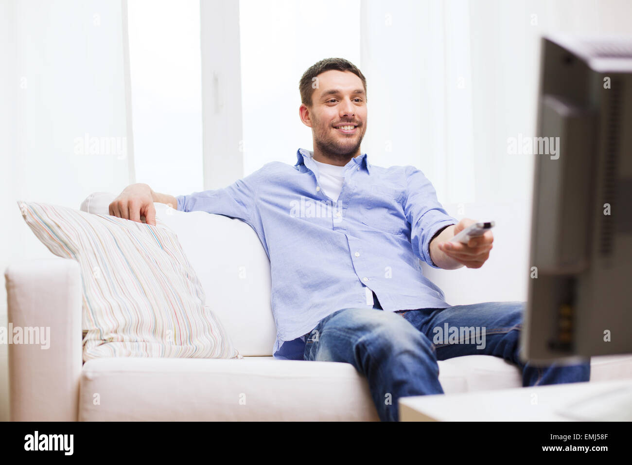 Handsome young man holding remote control and changing tv channels hi ...