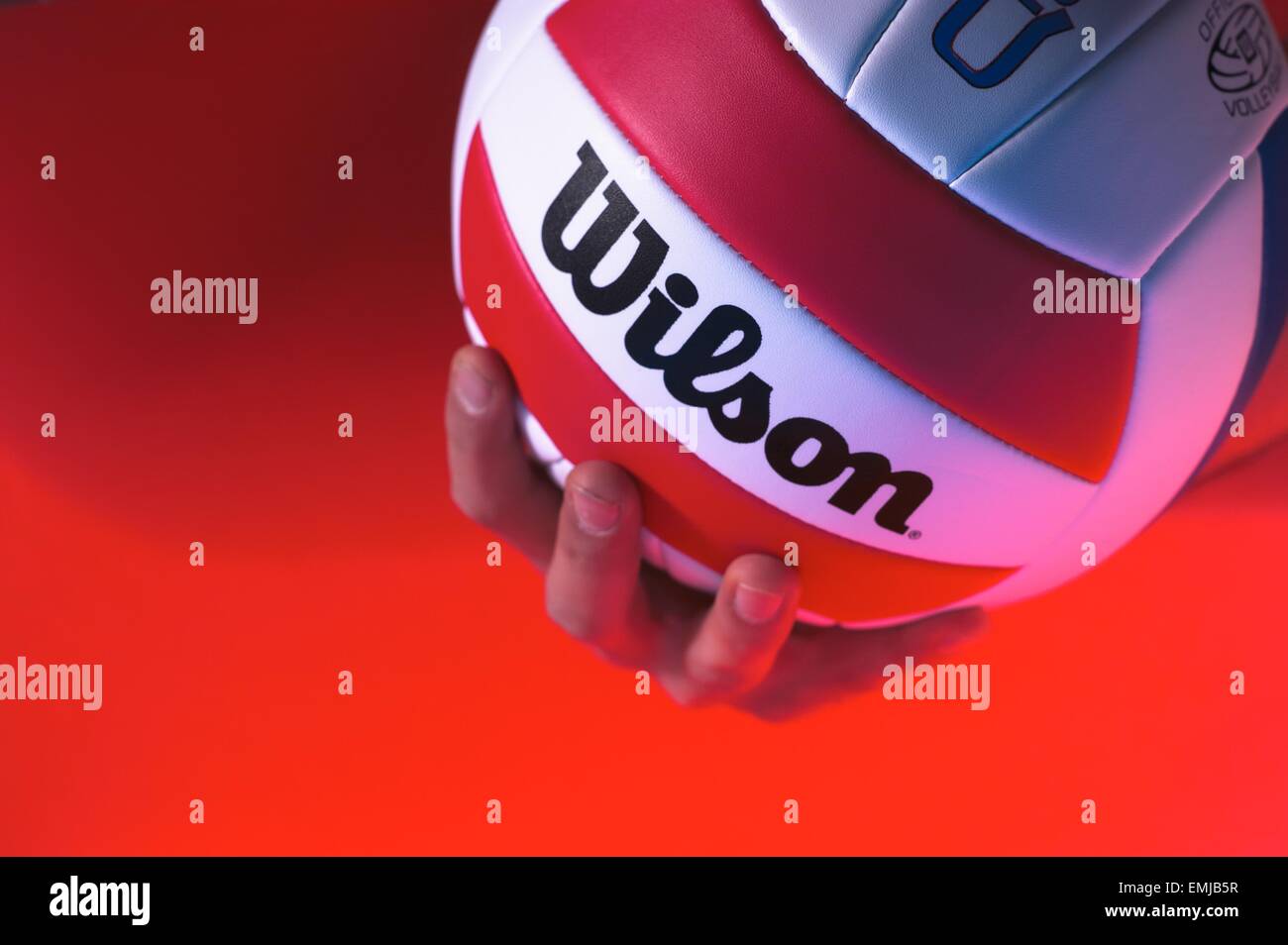 Hand holding a Wilson ball against a red background Stock Photo - Alamy