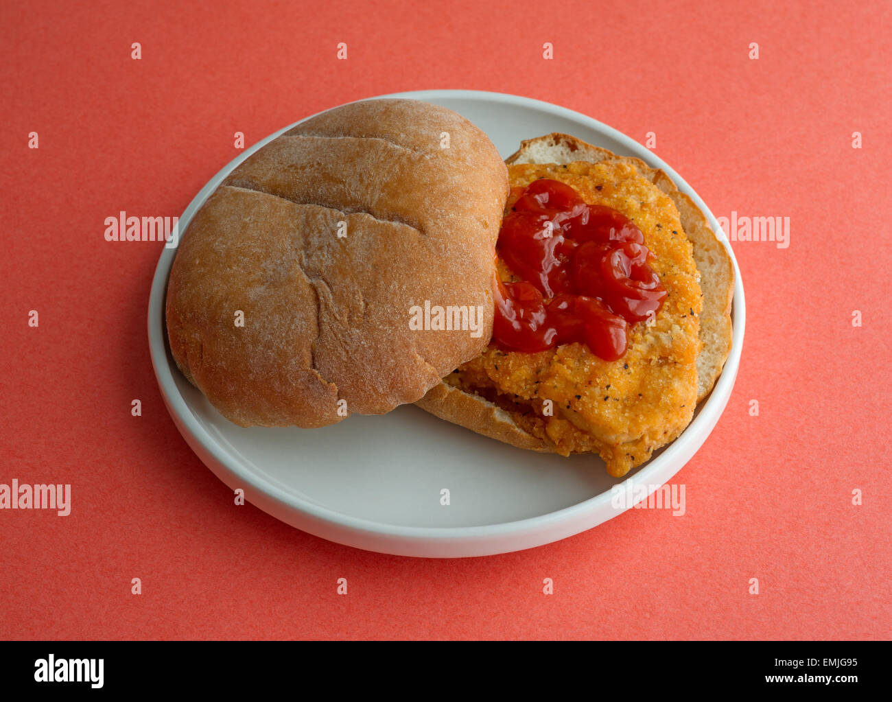 A freshly cooked breaded chicken sandwich with ketchup on a small plate ...