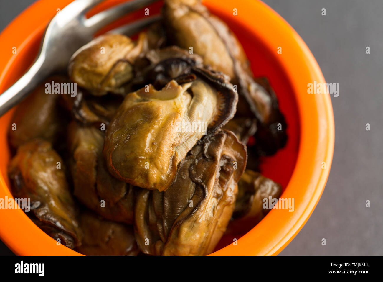 A very close view of small whole smoked oysters in a bright orange bowl ...