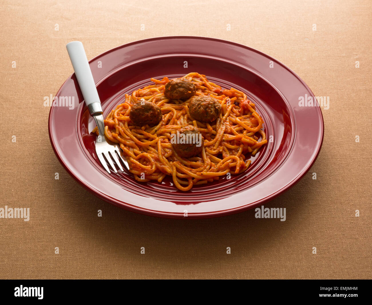 A spaghetti and meatball TV dinner on a red plate with a fork on a tan ...