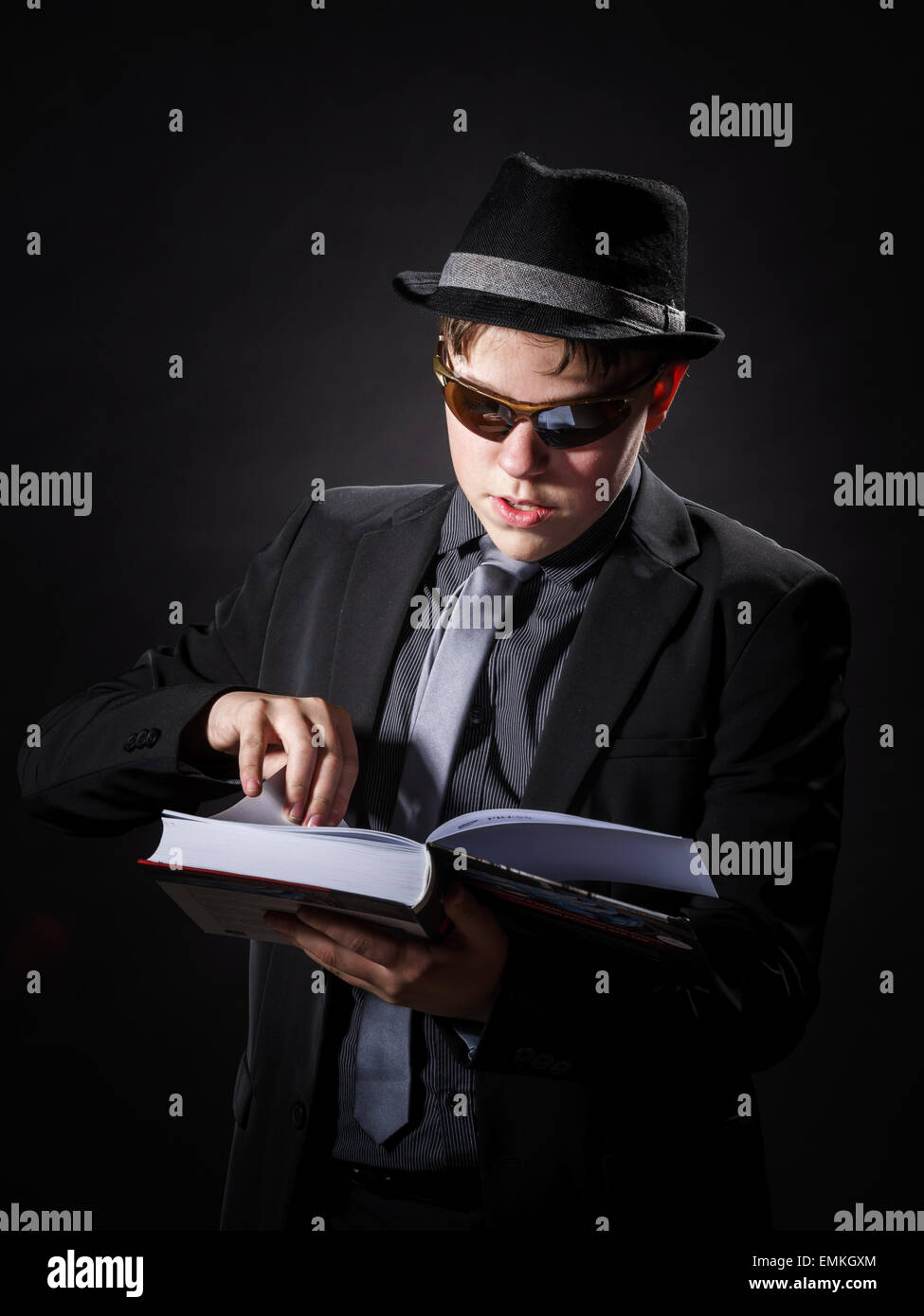 Seriously teenage boy dressed in suit reading book, isolated on black ...