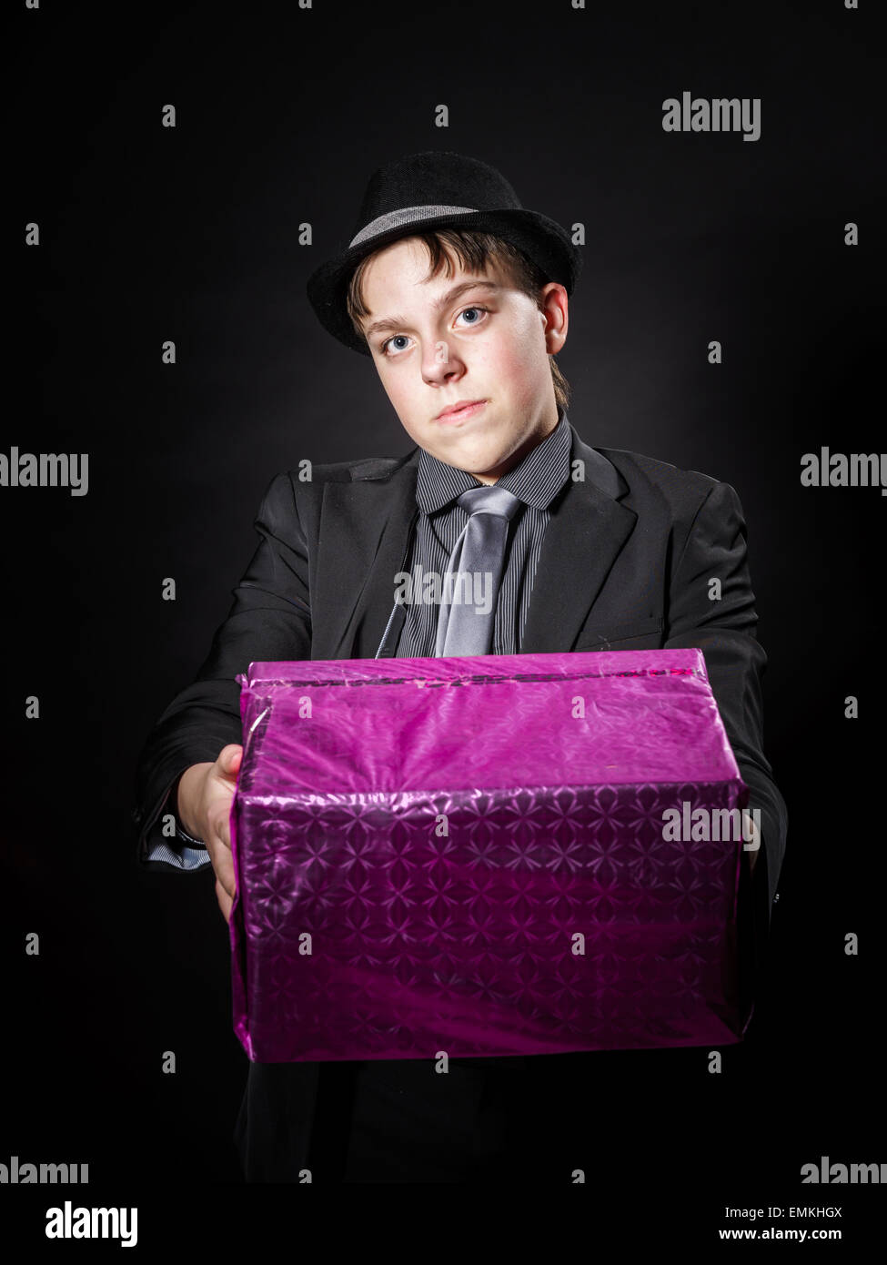 Expressive teenage boy holding box with gift isolated on black Stock ...