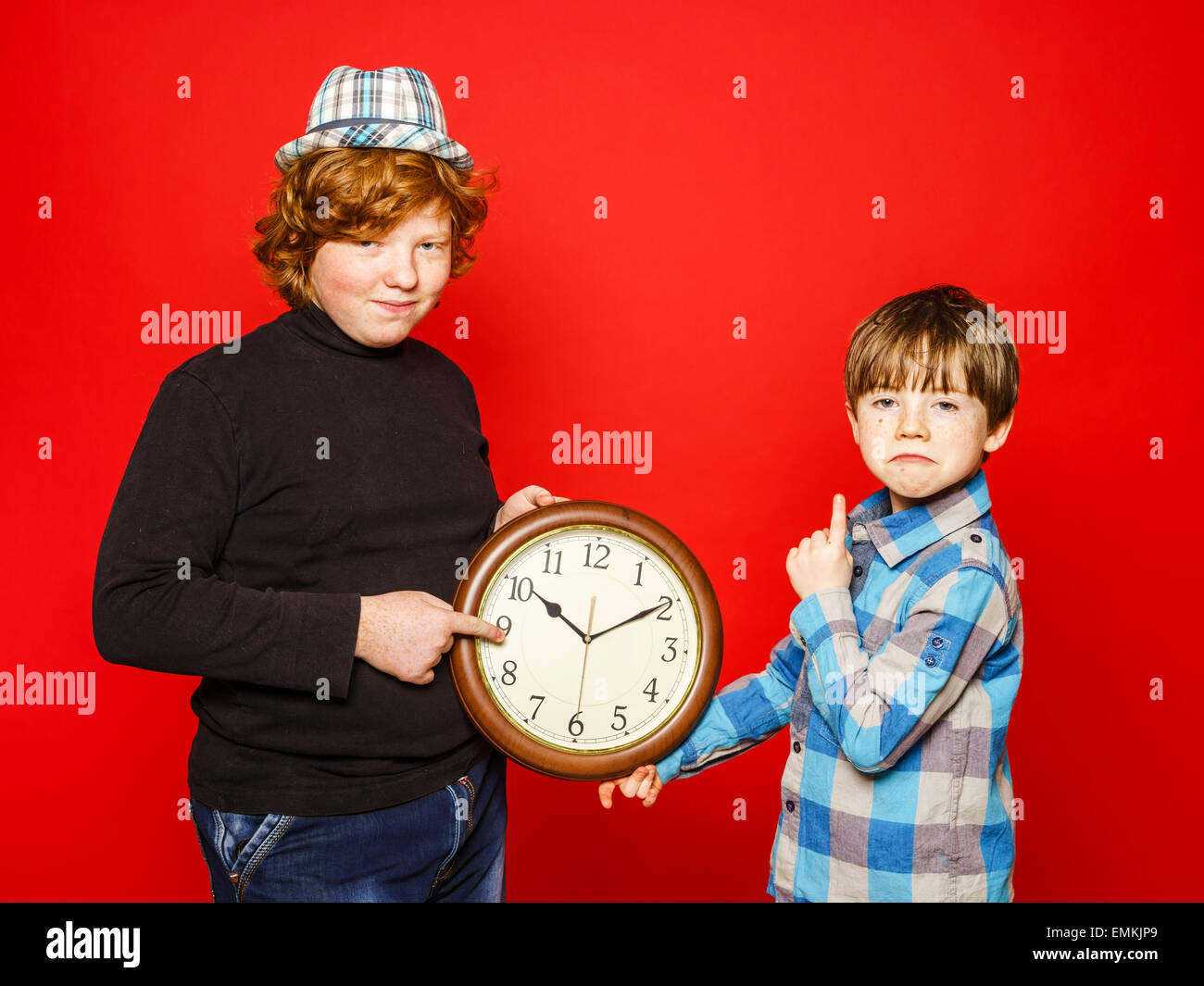Two red-hair brothers posing with big clock, isolated on red Stock ...