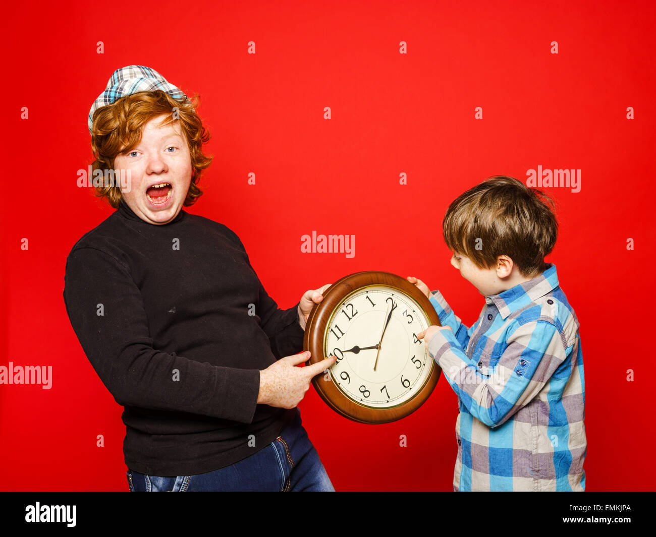 Two red-hair brothers posing with big clock, isolated on red Stock ...