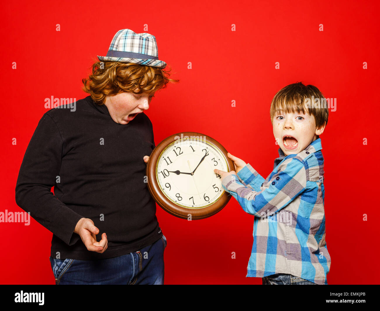 Two red-hair brothers posing with big clock, isolated on red Stock ...