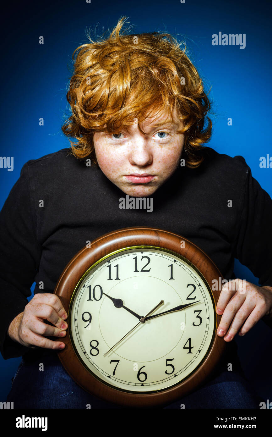 Expressive red-haired teenage boy showing time on big clock, business ...