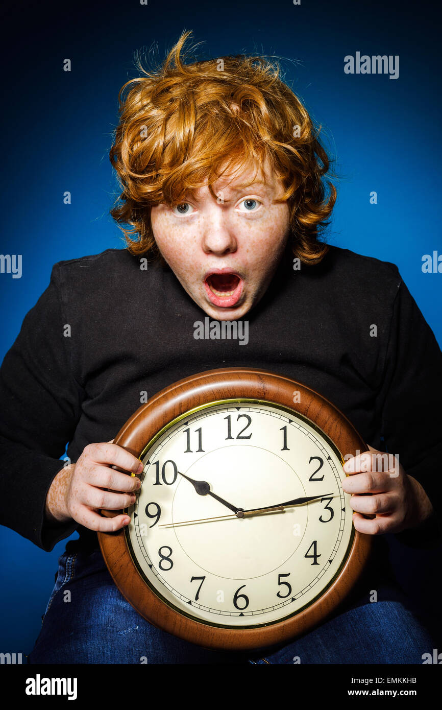Expressive red-haired teenage boy showing time on big clock, business ...