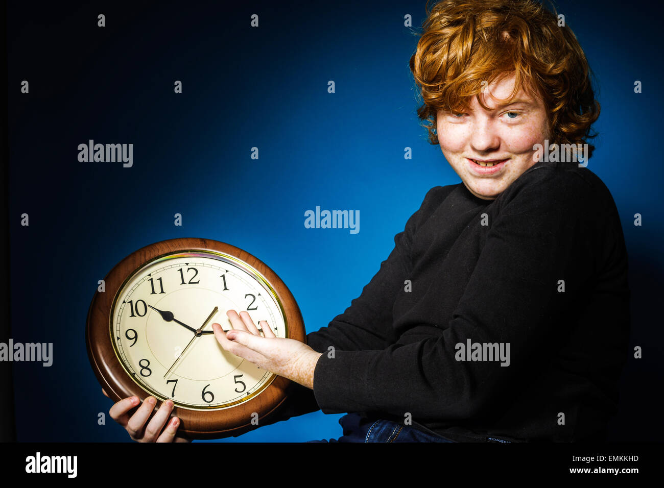 Expressive red-haired teenage boy showing time on big clock, business ...