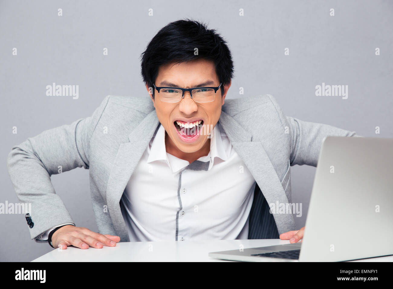 Angry young man sitting at the table with laptop and screaming on ...