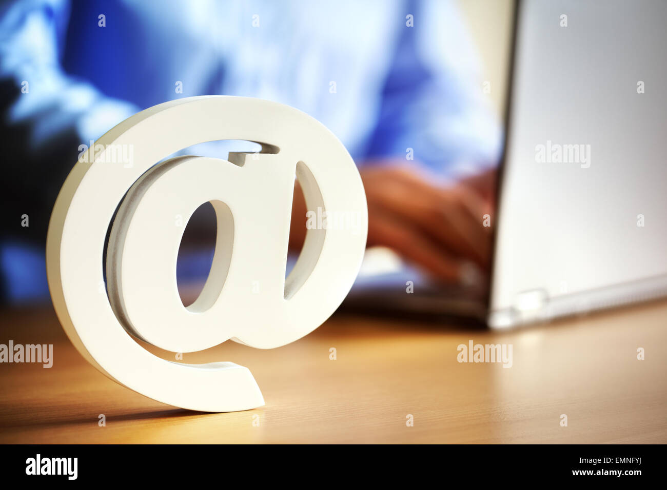 E-mail @ at symbol on an office desk with man on laptop computer Stock ...