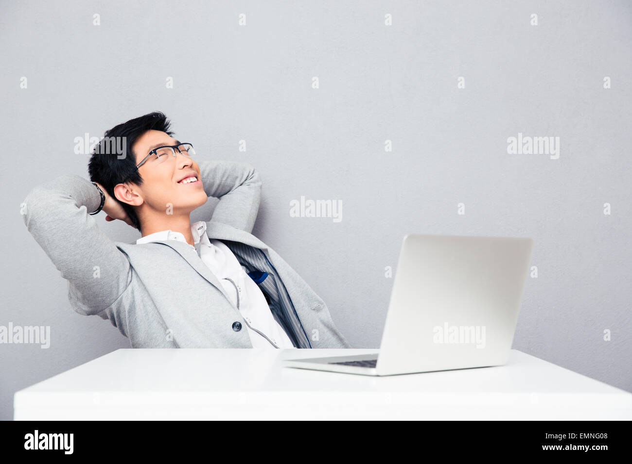 Happy young businessman resting at the table with laptop over gray ...