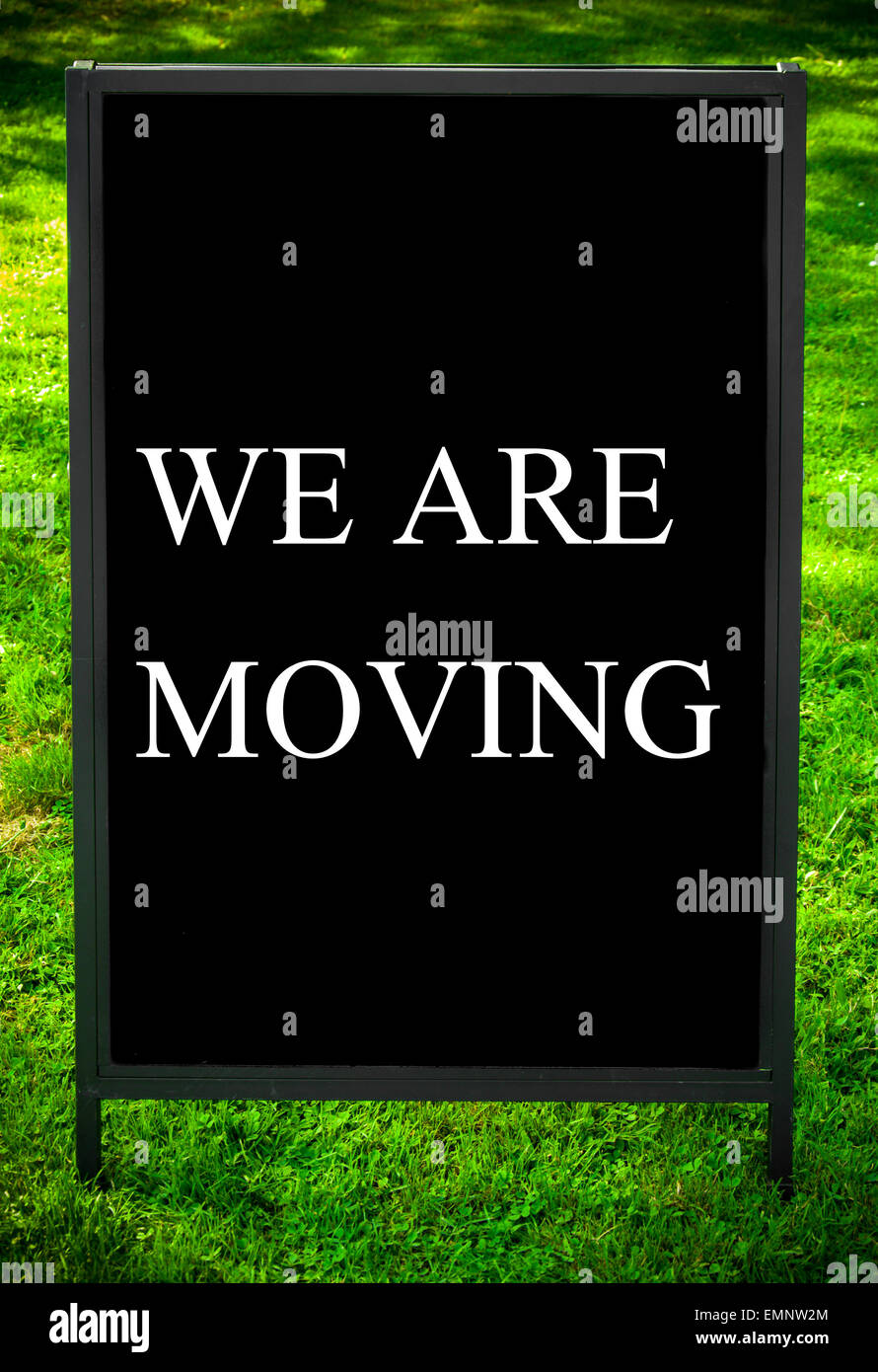 WE ARE MOVING message on sidewalk blackboard sign against green grass ...