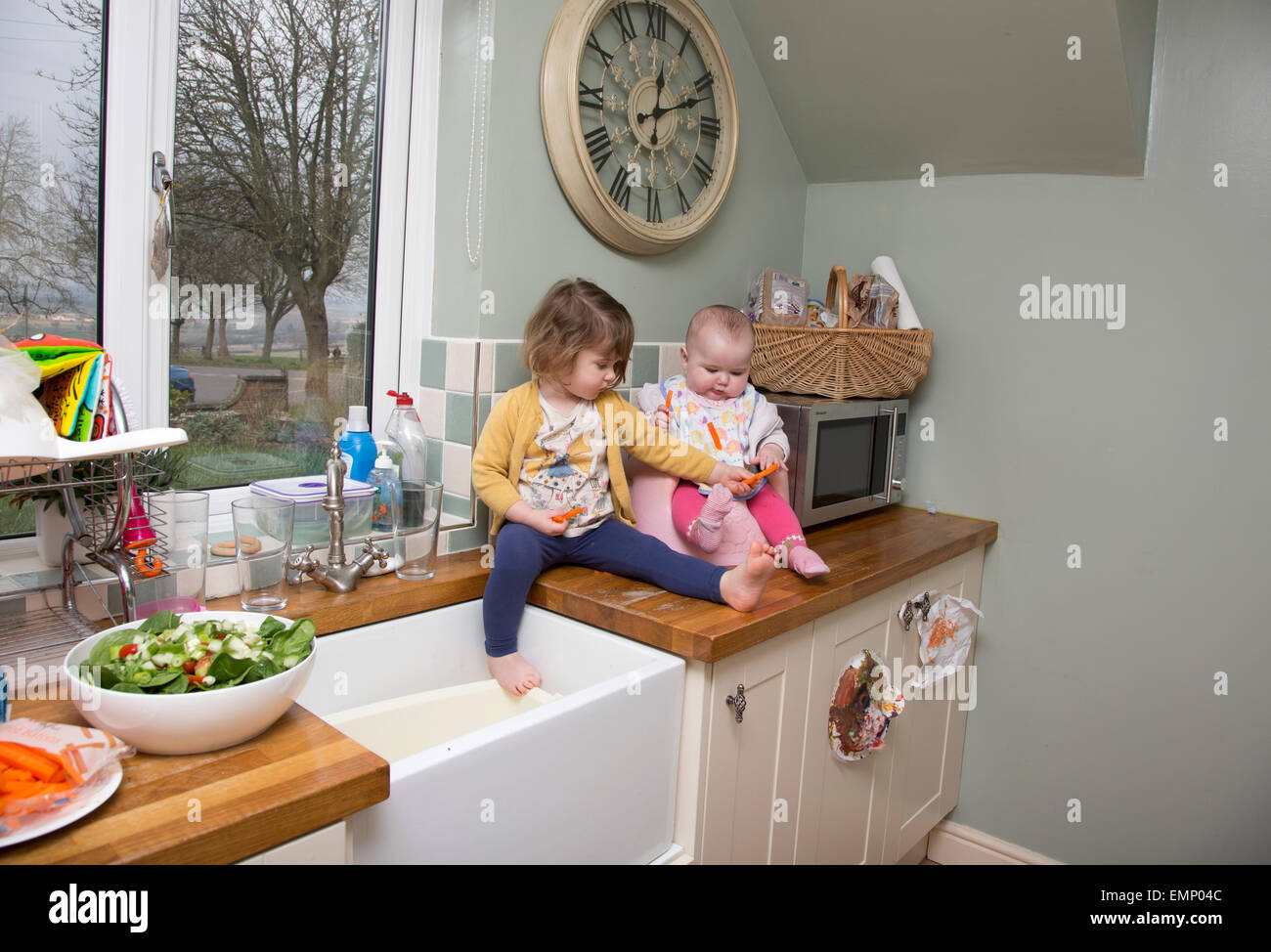 A toddler and baby sitting on a worktop in a kitchen Stock Photo - Alamy