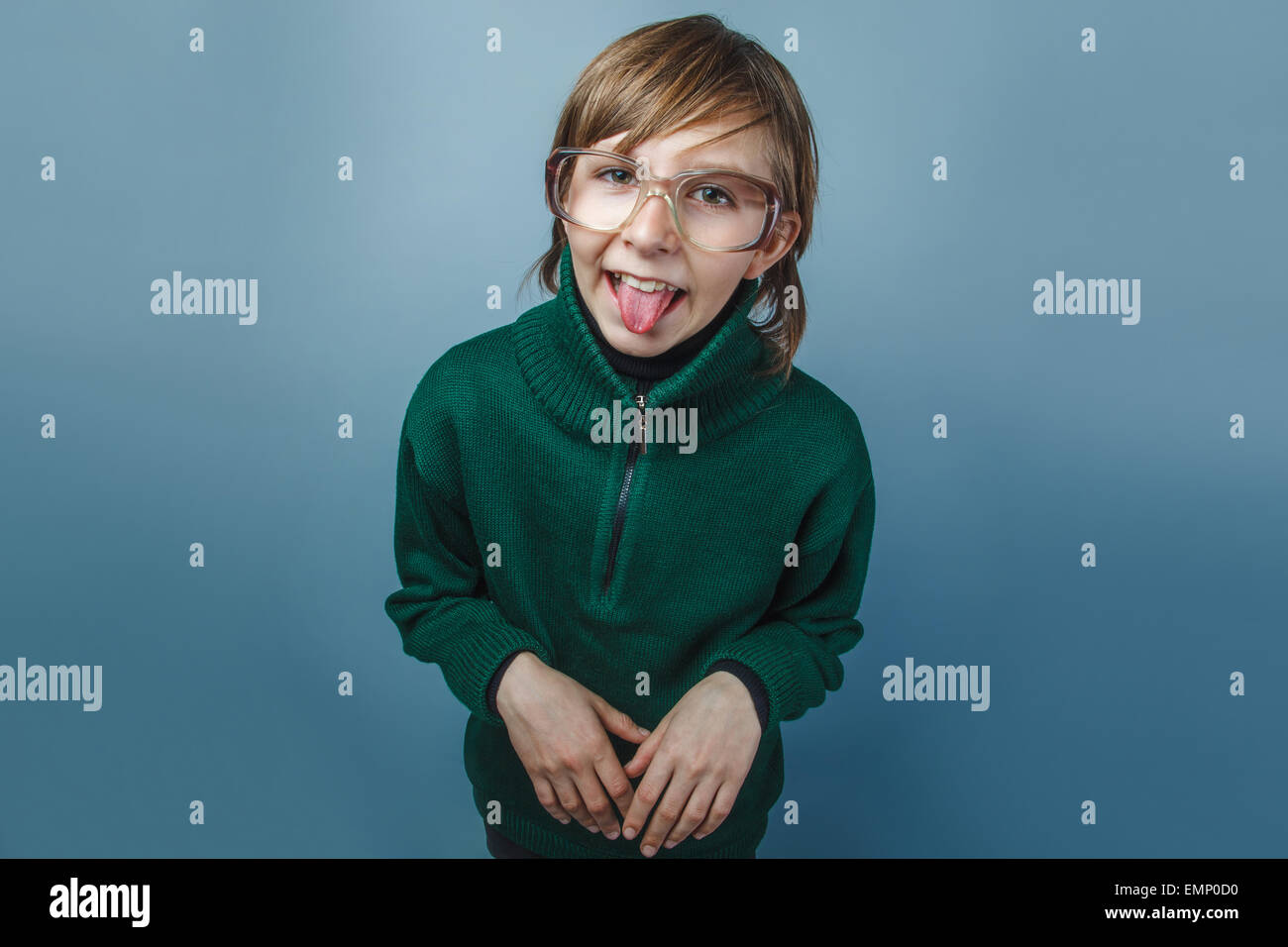 European-looking boy of ten years in glasses showing tongue on a gray ...