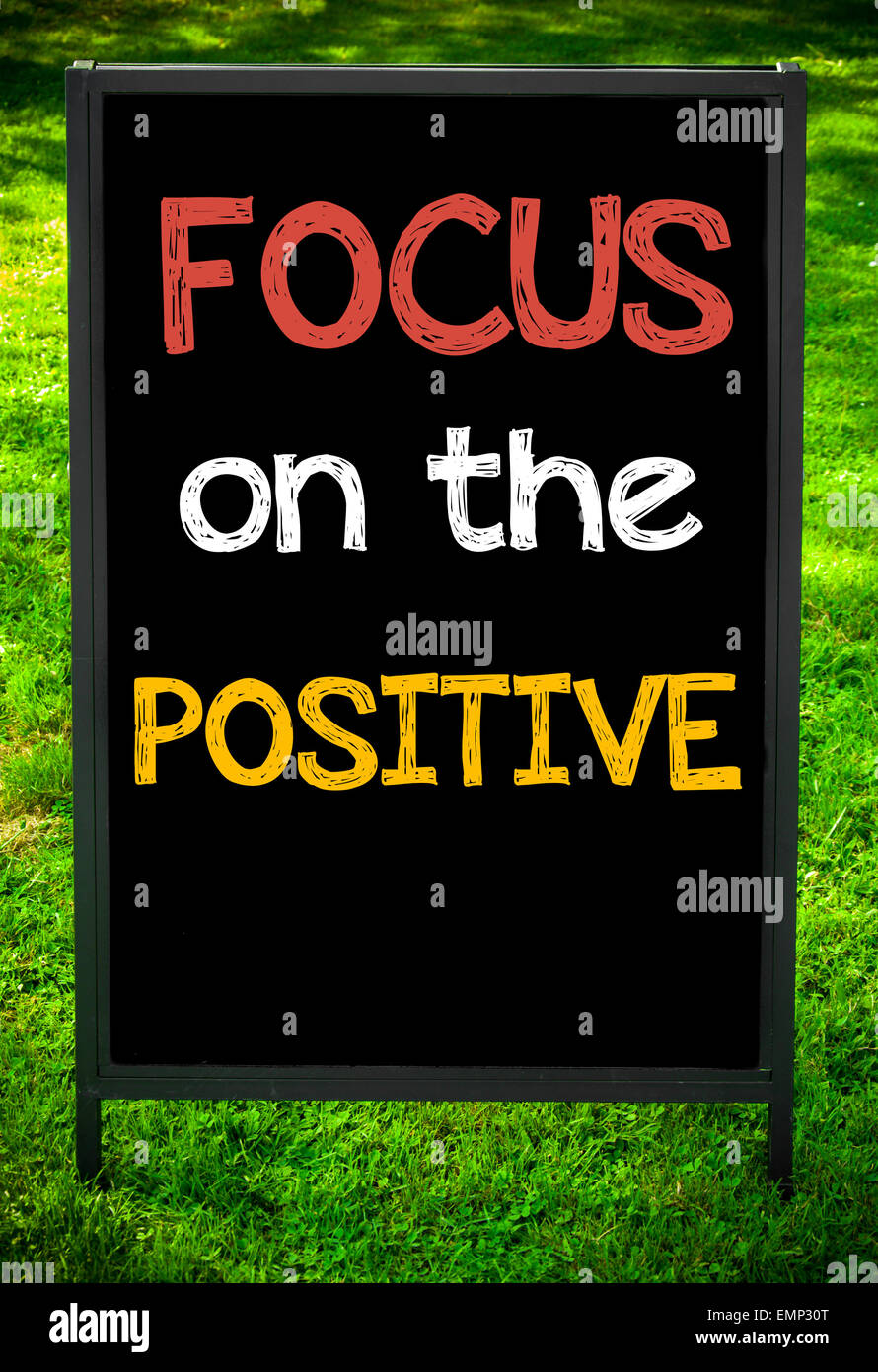 FOCUS ON THE POSITIVE message on sidewalk blackboard sign against green ...