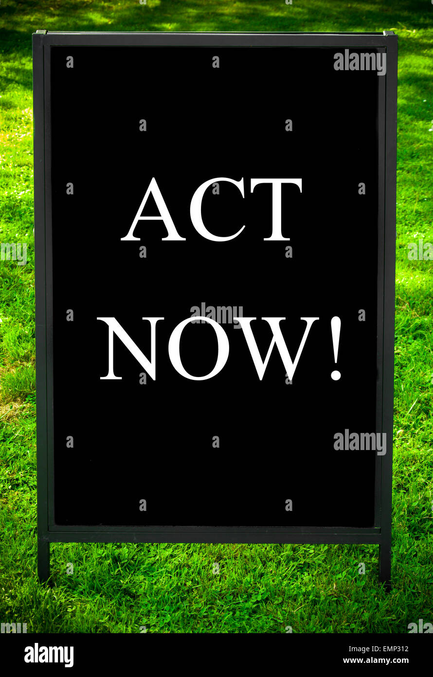 ACT NOW! message on sidewalk blackboard sign against green grass ...