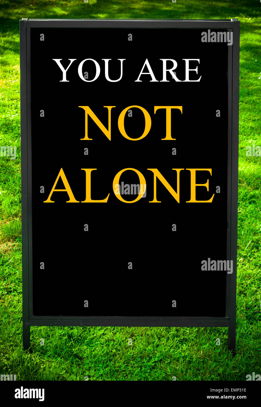 YOU ARE NOT ALONE message on sidewalk blackboard sign against green ...