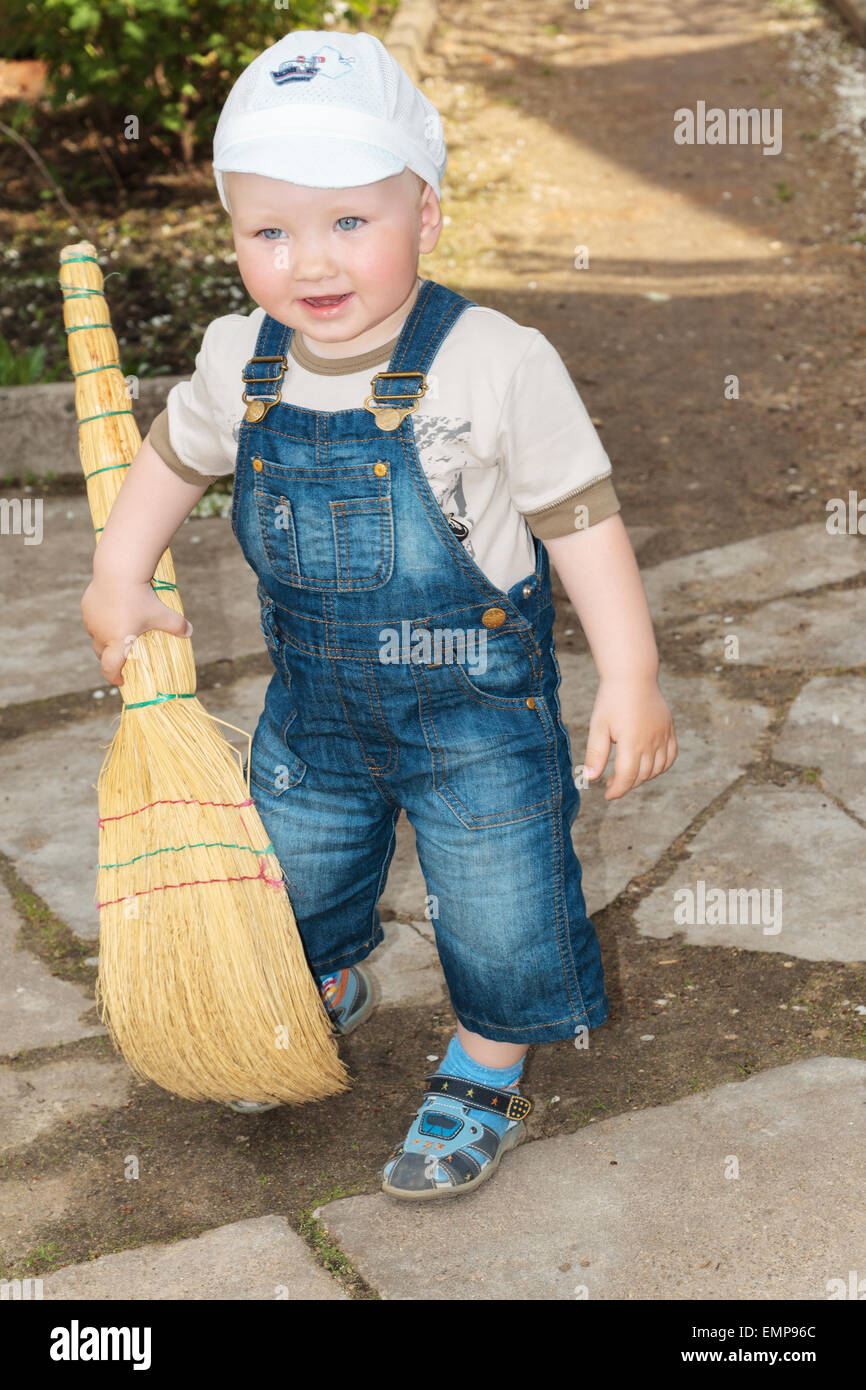 The little boy in a cap and a jeans suit with a broom in hands Stock ...