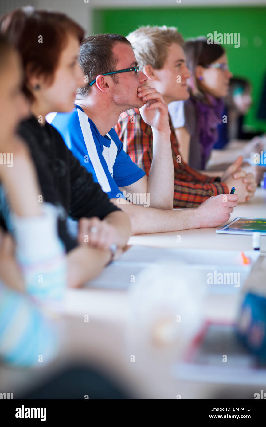 Handsome college student sitting in a classroom full of students during ...