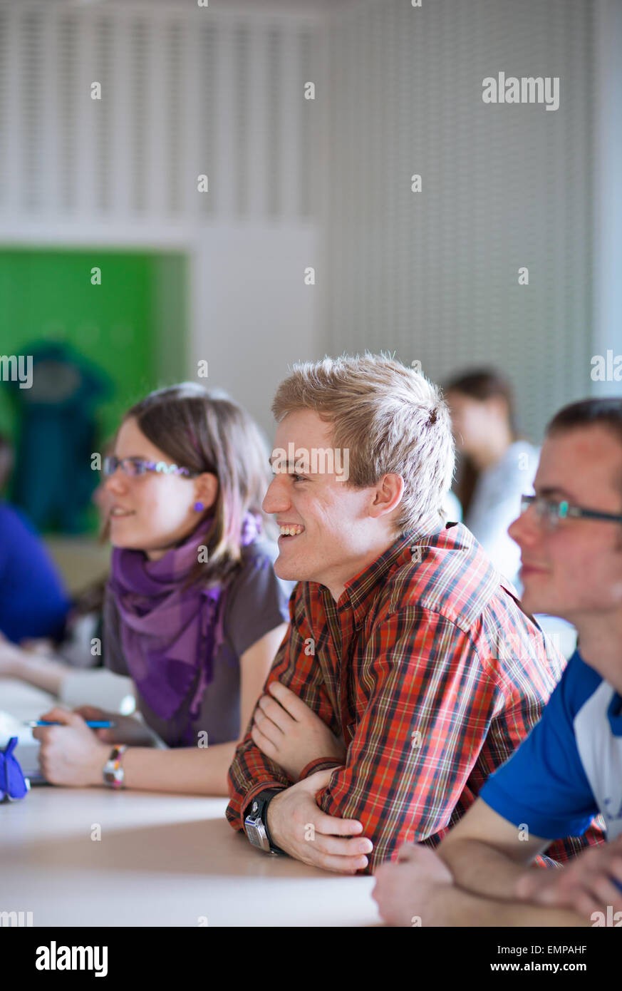 Handsome college student sitting in a classroom full of students during ...