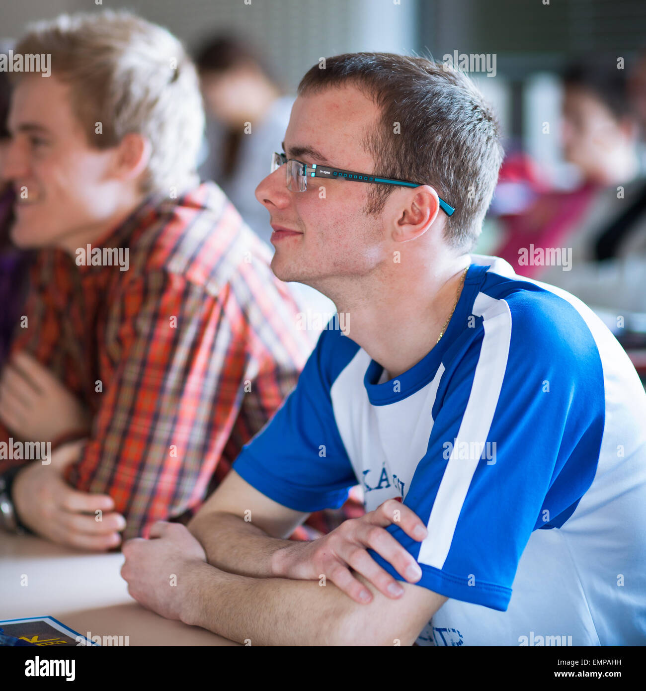 Handsome college student sitting in a classroom full of students during ...