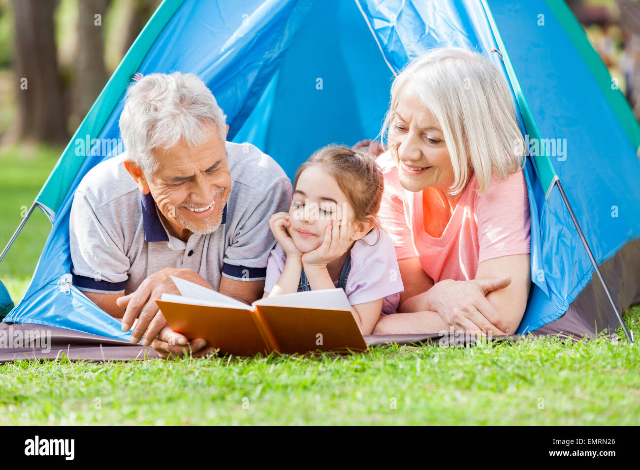 Grandparent With Granddaughter Reading Book At Campsite Stock Photo - Alamy