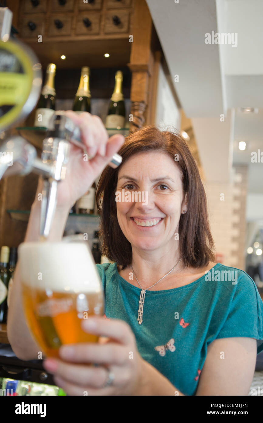 A woman behind a bar pulling a pint of lager while smiling Stock Photo ...