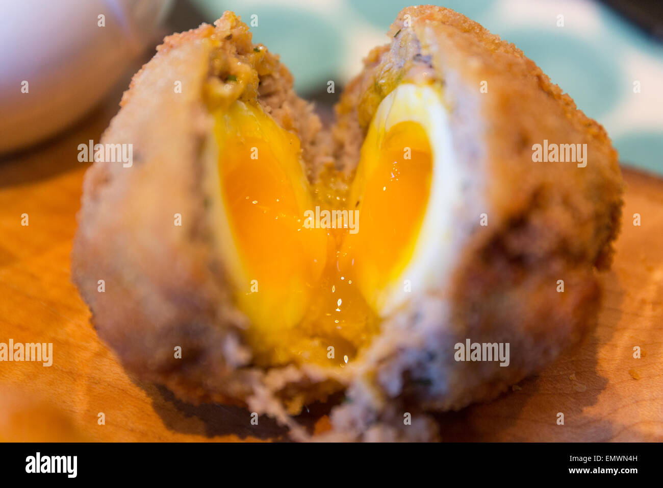 A soft boiled scotch egg cut open to show the egg gently pouring out of ...