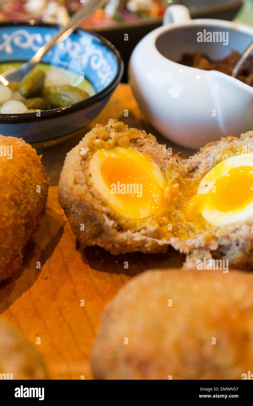 A soft boiled scotch egg cut open to show the egg gently pouring out of ...