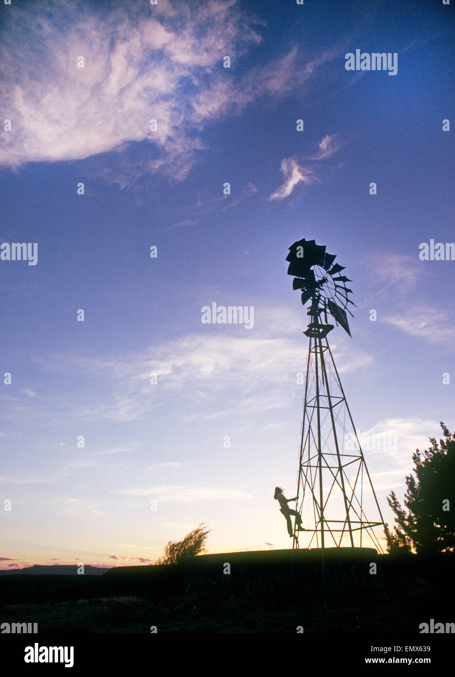 A ranch girl climbs a windmill at sunset in the remote cattle country ...
