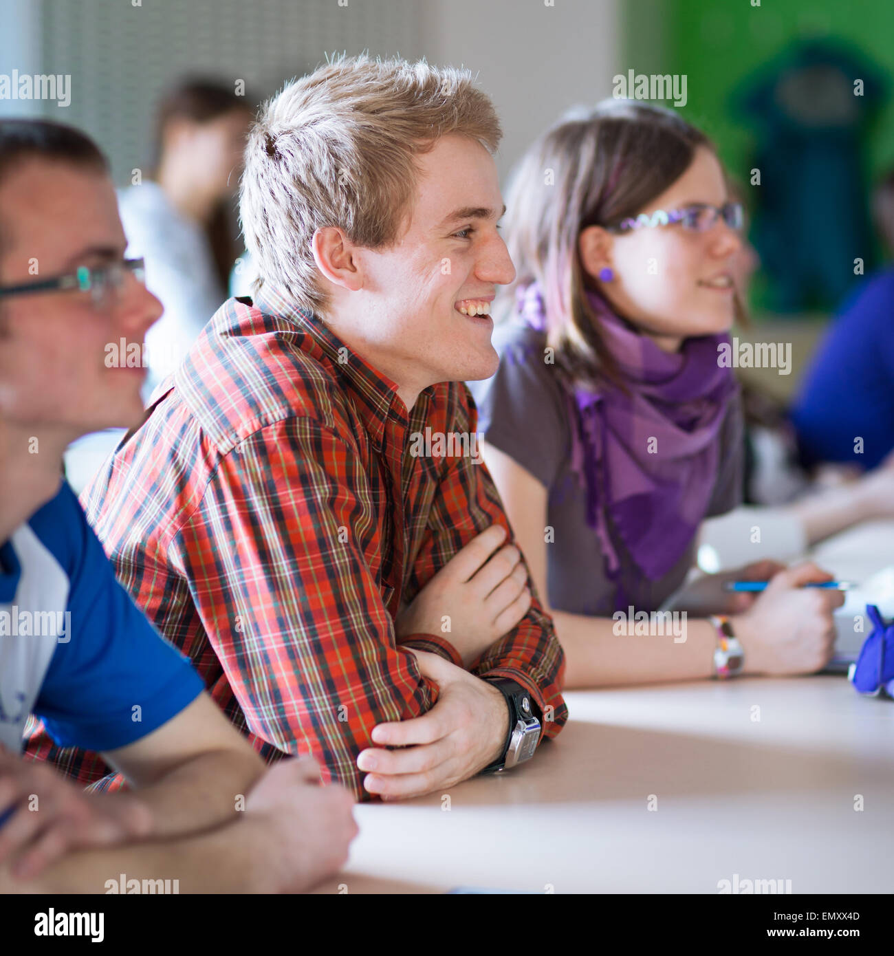 Handsome college student sitting in a classroom full of students during ...