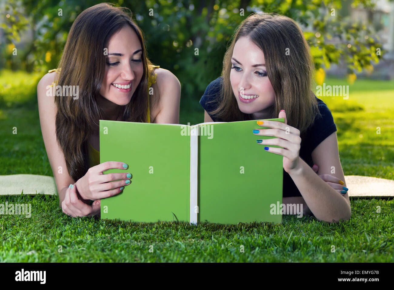 Two young happy smiling girls reading a book in a summer green p Stock ...